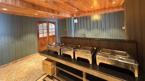 Uma área de buffet com teto de madeira e paredes azuis, com bandejas de servir em aço inoxidável e uma porta de madeira.