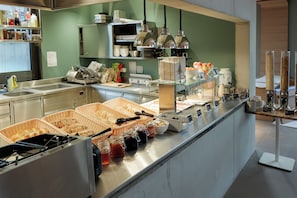 Espaço de buffet de café da manhã com pães, geleias e estação de café.