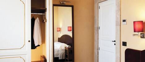 Quarto de hotel com guarda-roupa, cama, mesa de cabeceira, espelho e luminária na parede.