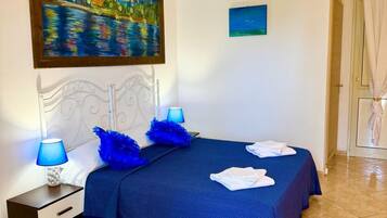 Um quarto com cama, mesas de cabeceira, um quadro e vista para o mar.