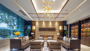 Um lobby moderno com área de sofás, lareira e uma grande janela com vista para o verde.