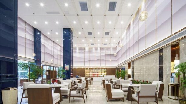 Um hall amplo com várias áreas de estar, uma receção central e uma grande janela com vista para o exterior.