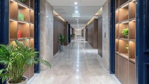 Corredor moderno de hotel com piso de mármore, estantes de madeira com plantas e iluminação embutida.