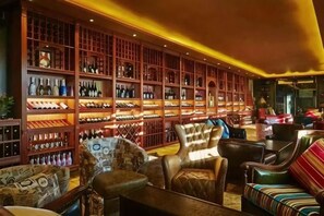 Zona de bar com prateleiras de garrafas, assentos de couro e ambiente acolhedor.