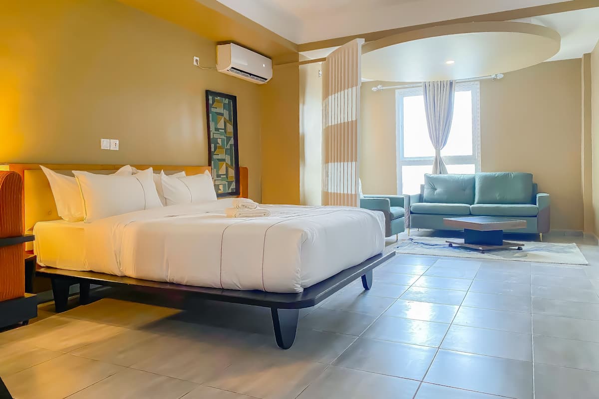 Quarto de hotel com cama, sofá, janela com cortinas e ar condicionado.