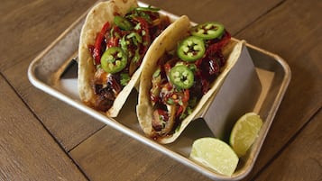 Dois tacos com jalapeños e gomos de limão em uma bandeja de metal.