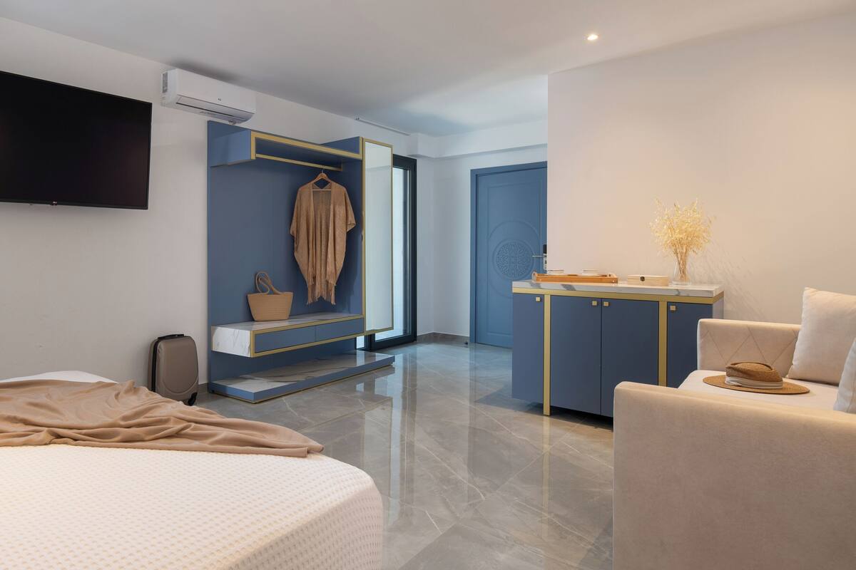 Quarto de hotel moderno com cama, área de estar com mesa, guarda-roupa e televisão na parede.