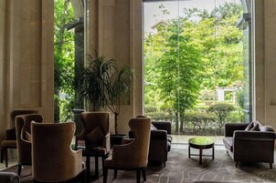 Um hall com várias áreas de estar, uma janela ampla com vista para o verde e um vaso de planta.