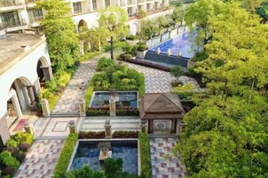 Pátio com uma fonte central, rodeado por vegetação e uma piscina.