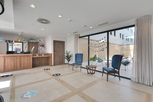 Um saguão moderno de hotel com balcão de recepção, área de estar e grandes janelas que oferecem vistas do interior do edifício.