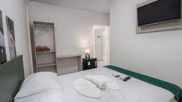 Quarto de hotel com cama, televisão na parede, guarda-roupa e mesa de cabeceira com abajur.