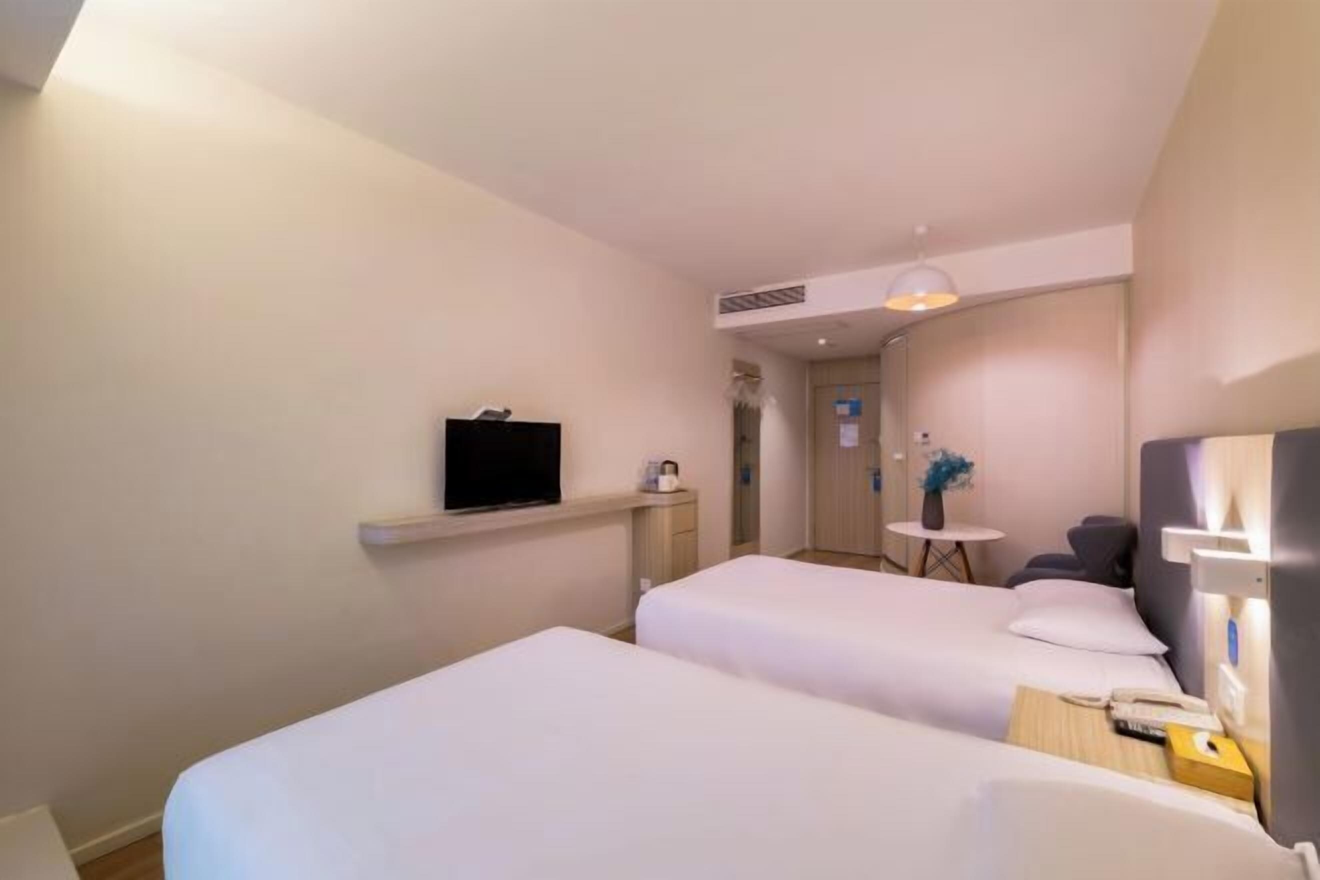 Quarto de hotel com duas camas, televisão, mesa pequena com abajur e escrivaninha com cadeira.