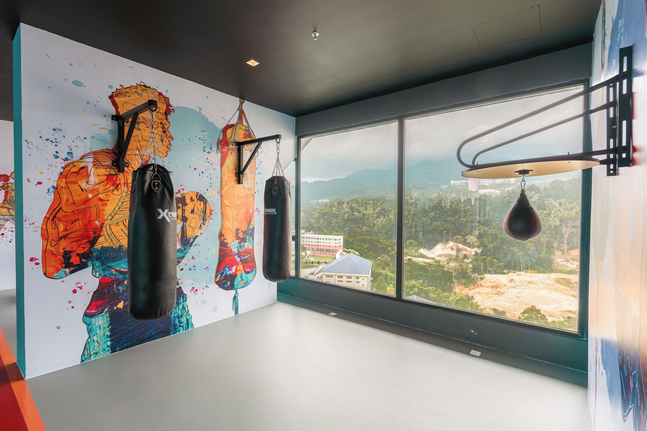 Academia com janelas amplas, um mural e sacos de pancada.