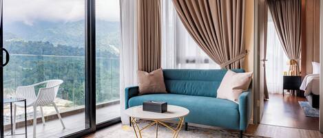 Quarto de hotel moderno com uma janela grande, um sofá verde-água, uma mesa de centro redonda e vista para uma paisagem montanhosa.