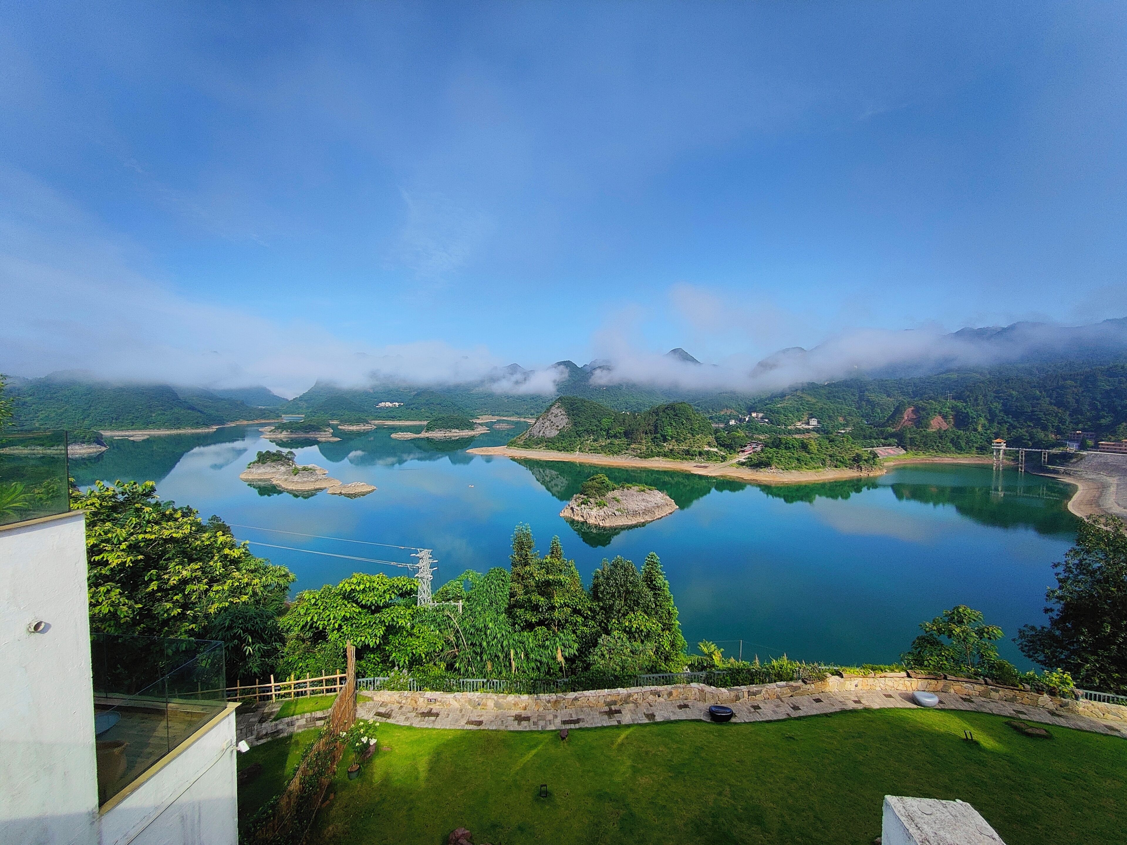 Vista panorâmica de um lago tranquilo rodeado por vegetação exuberante e montanhas, sob um céu claro.