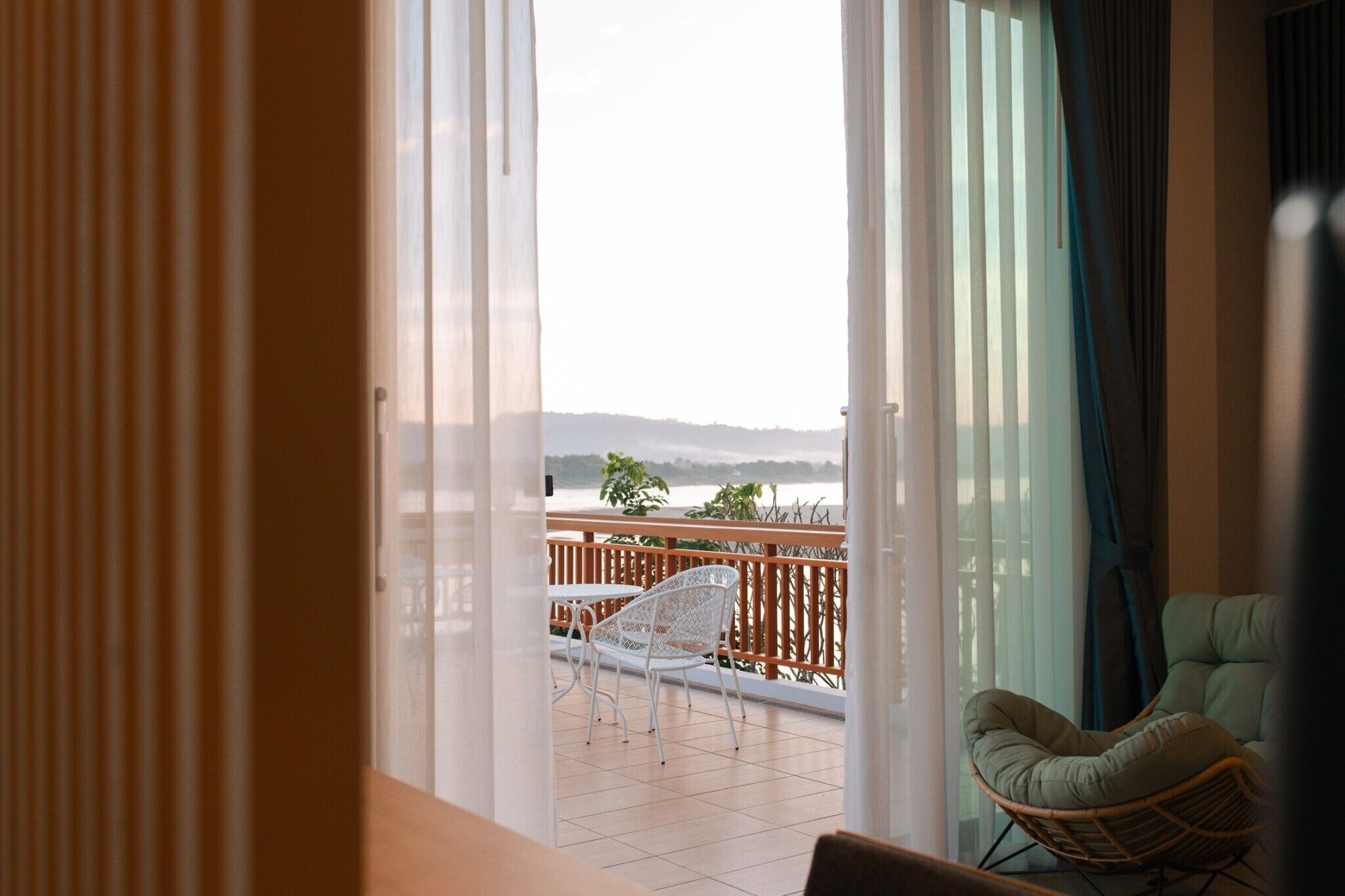 Varanda com vista para um lago e colinas distantes, equipada com uma cadeira e uma mesa.