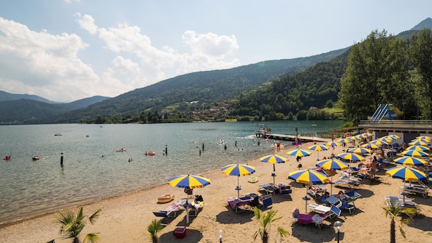 Uma praia com guarda-sóis, espreguiçadeiras e um lago.