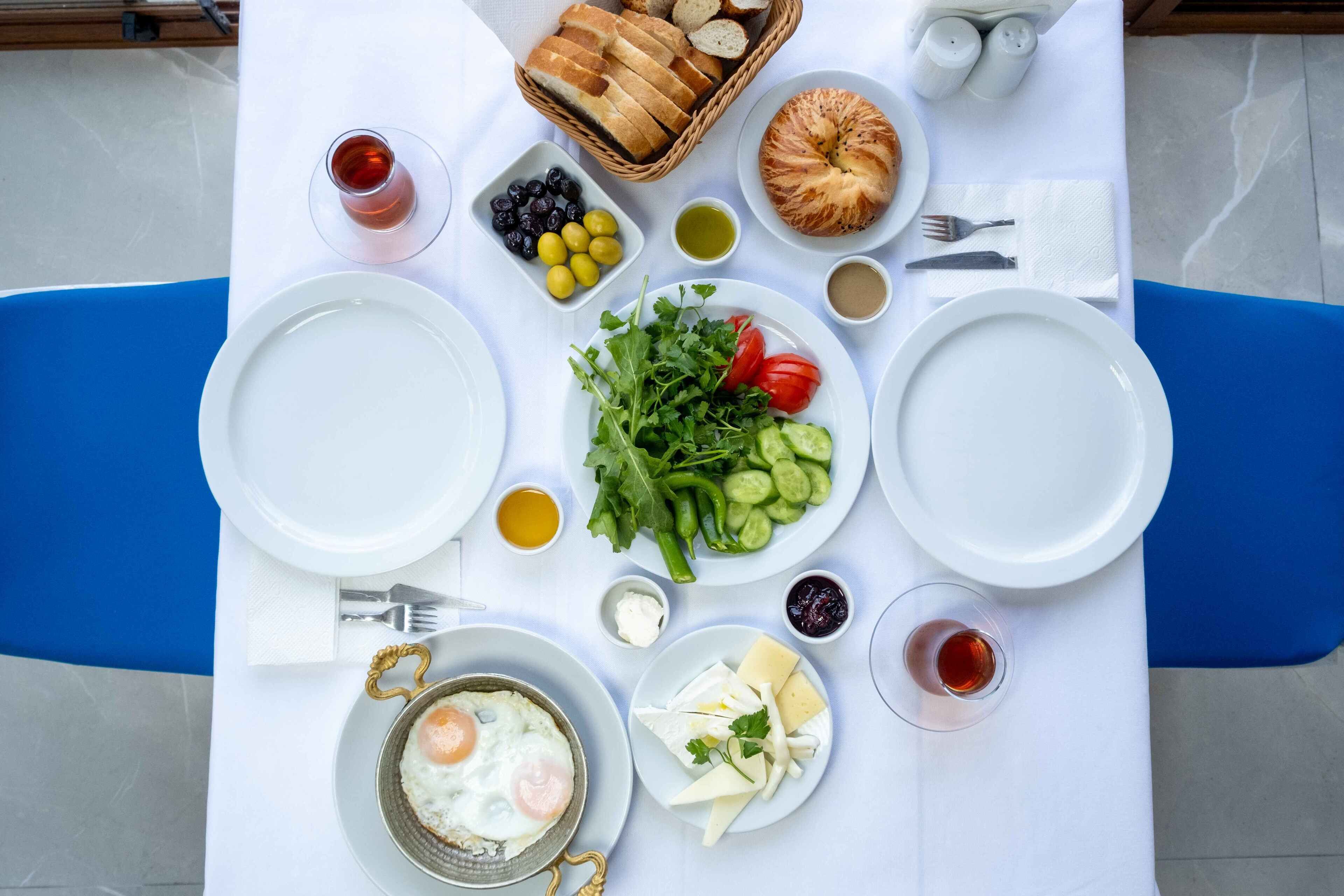 Mesa de café da manhã com pratos, pão, ovos e diversos acompanhamentos.