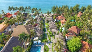 Um resort com piscina, bangalôs de palha, palmeiras e vista para o oceano.