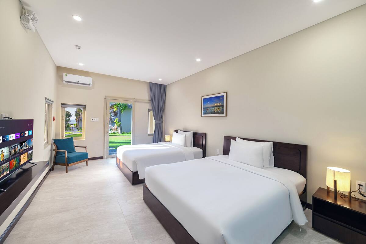 Quarto de hotel com duas camas, televisão, escrivaninha e vista para o exterior.
