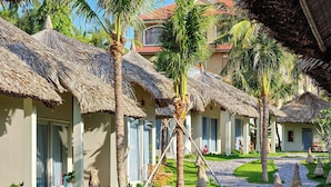 Um resort com cabanas de telhado de palha, um caminho pavimentado e palmeiras.