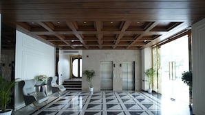 Um lobby moderno com piso de mármore geométrico, vigas de madeira no teto e uma área de estar com cadeiras e uma mesa.