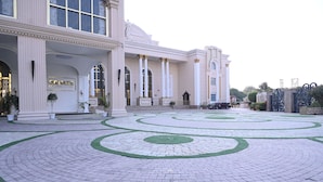 Uma entrada imponente com uma entrada circular, uma placa com a inscrição "GRATE COASTAL GLORY" e um prédio grande com colunas e janelas em arco.