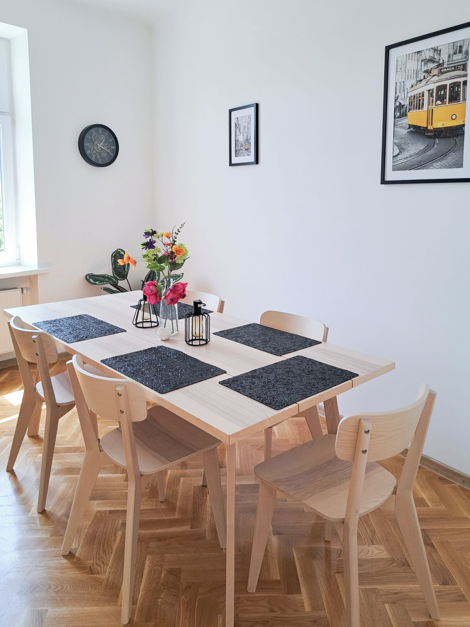 Uma área de refeições com uma mesa e cadeiras de madeira, um vaso com flores e um quadro na parede.