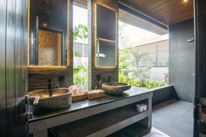 Uma casa de banho moderna com duas grandes pias de pedra, toucador de madeira e um espelho grande.