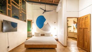 Quarto com cama de madeira, ventilador de teto e uma grande obra de arte abstrata na parede.