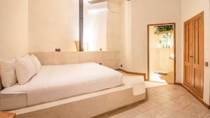 Quarto com uma cama, uma porta de madeira e uma planta pequena no canto.