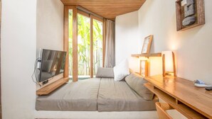 Quarto com cama, TV, escrivaninha de madeira e janela com vista para o verde.