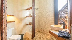 Casa de banho moderna com sanita, chuveiro e lavatório. Existem prateleiras com artigos de higiene e um porta-toalhas.