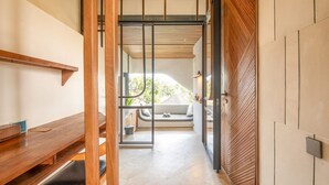 Um interior moderno com um banco de madeira, uma porta de vidro que dá para uma varanda e vista para o verde lá fora.