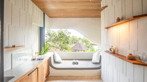 Uma cozinha moderna com um assento embutido junto à janela, armários de madeira e vista para o verde lá fora.