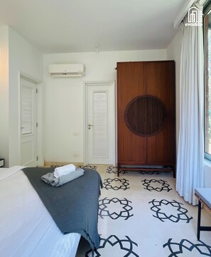 Quarto de hotel com uma cama, um guarda-roupa, um ar condicionado e um chão estampado.