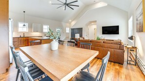 Uma sala de estar ampla com uma mesa de jantar de madeira, um sofá de couro marrom e uma televisão de tela plana na parede.
