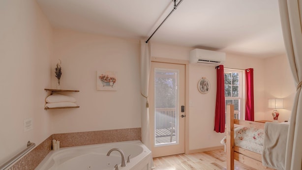 Casa de banho com banheira, chuveiro, sanita e lavatório. Tem uma janela com cortinas vermelhas, unidade de ar condicionado e um porta-toalhas.