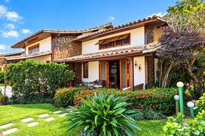 Uma casa de dois andares com fachada de pedra, telhado em telhas e um jardim bem cuidado com flores vermelhas e arbustos verdes.