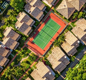 Vista aérea de um bairro residencial com várias casas, quadra de tênis e vegetação ao redor.