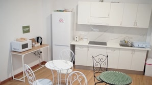 Uma cozinha compacta com armários brancos, micro-ondas, chaleira e um pequeno espaço de refeições com mesa redonda e cadeiras.