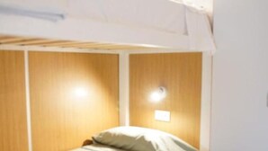 Quarto com beliche, guarda-roupa de madeira e uma pequena mesa de cabeceira com abajur.