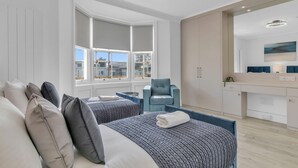 Quarto de hotel com duas camas, área de estar, escrivaninha e uma janela grande com vista para a cidade.