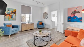 Uma sala de estar moderna com um sofá azul, um sofá laranja, uma mesa de centro e obras de arte nas paredes.