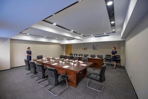 Uma sala de conferências com uma mesa comprida, cadeiras e piso coberto por carpete.