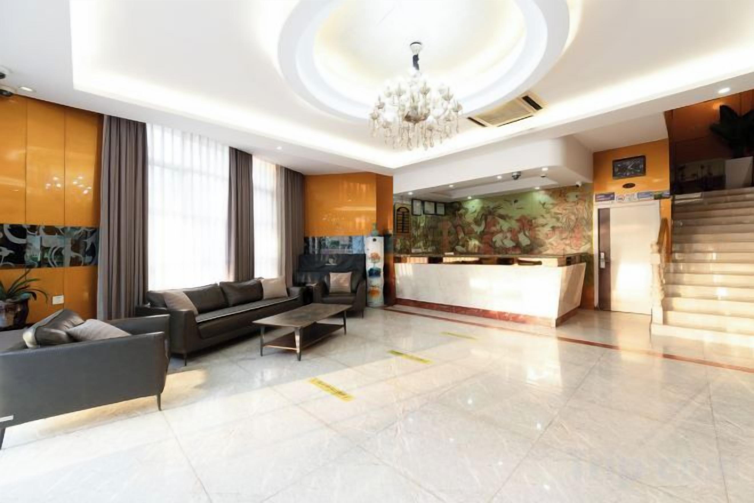 Um saguão de hotel com balcão de recepção, sofás, um candelabro e uma escadaria.