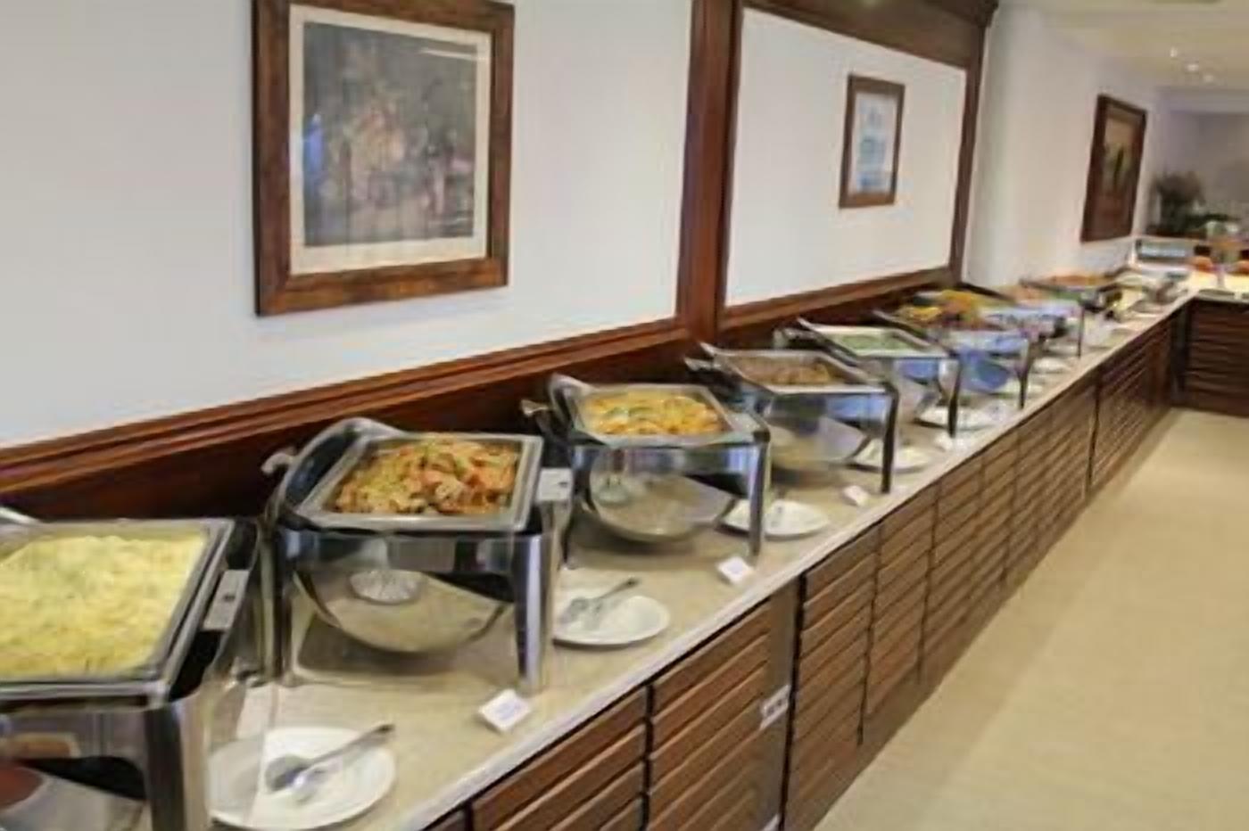 Buffet com diversas opções de comida, obras de arte nas paredes e um armário de madeira ao lado.