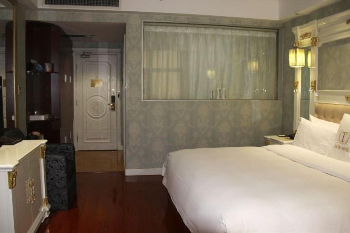 Quarto de hotel com uma cama grande, guarda-roupa, espelho e janela com cortinas.