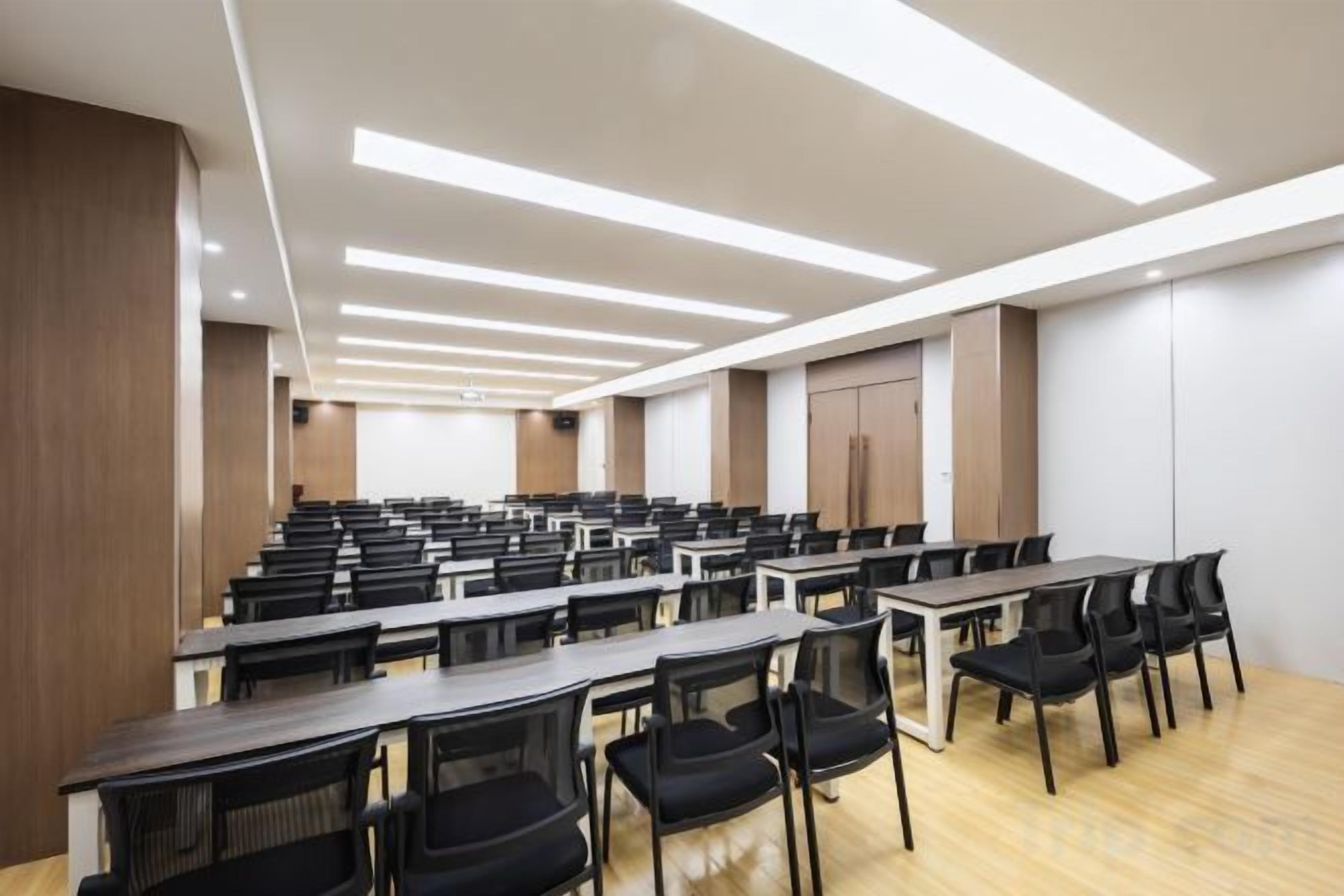 Sala de conferências com várias mesas e cadeiras, piso de madeira e design moderno no teto.