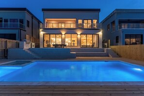 Uma casa moderna de dois andares com piscina, deck de madeira e interior bem iluminado.